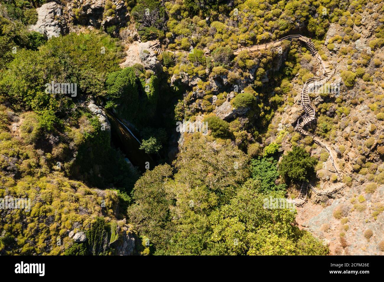 Aerial view of a waterfall in a narrow gorge next to winding wooden ...