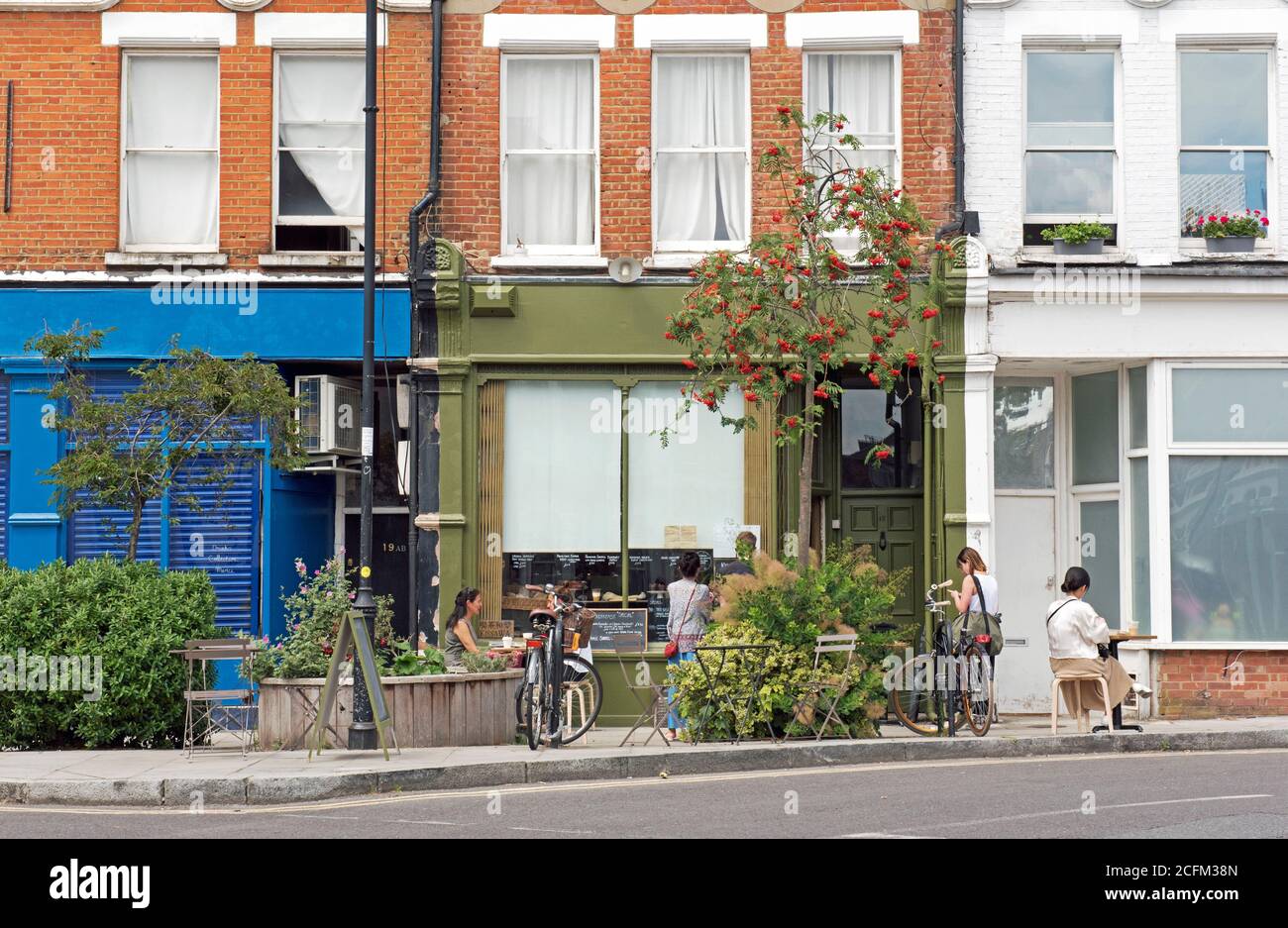 People sitting outside café in Highbury with plants and bikes, London ...
