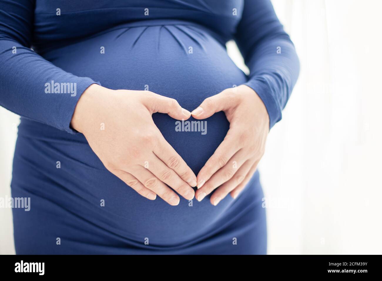 Pregnant woman hold heart-shaped hands on her baby bump. Bright photo ...