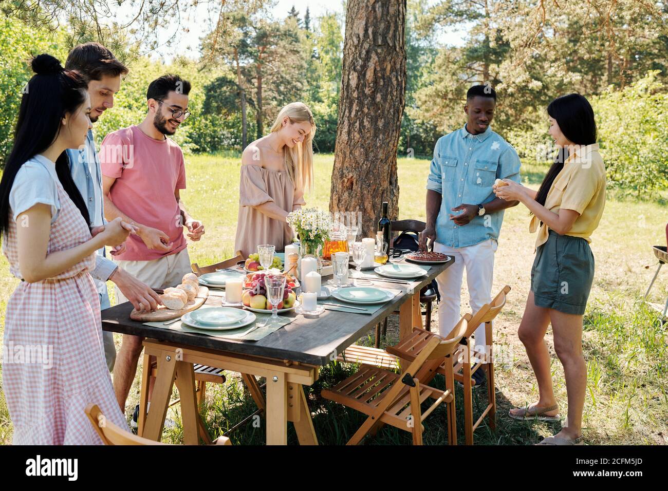 Large group of young intercultural friendly people standing under pine ...