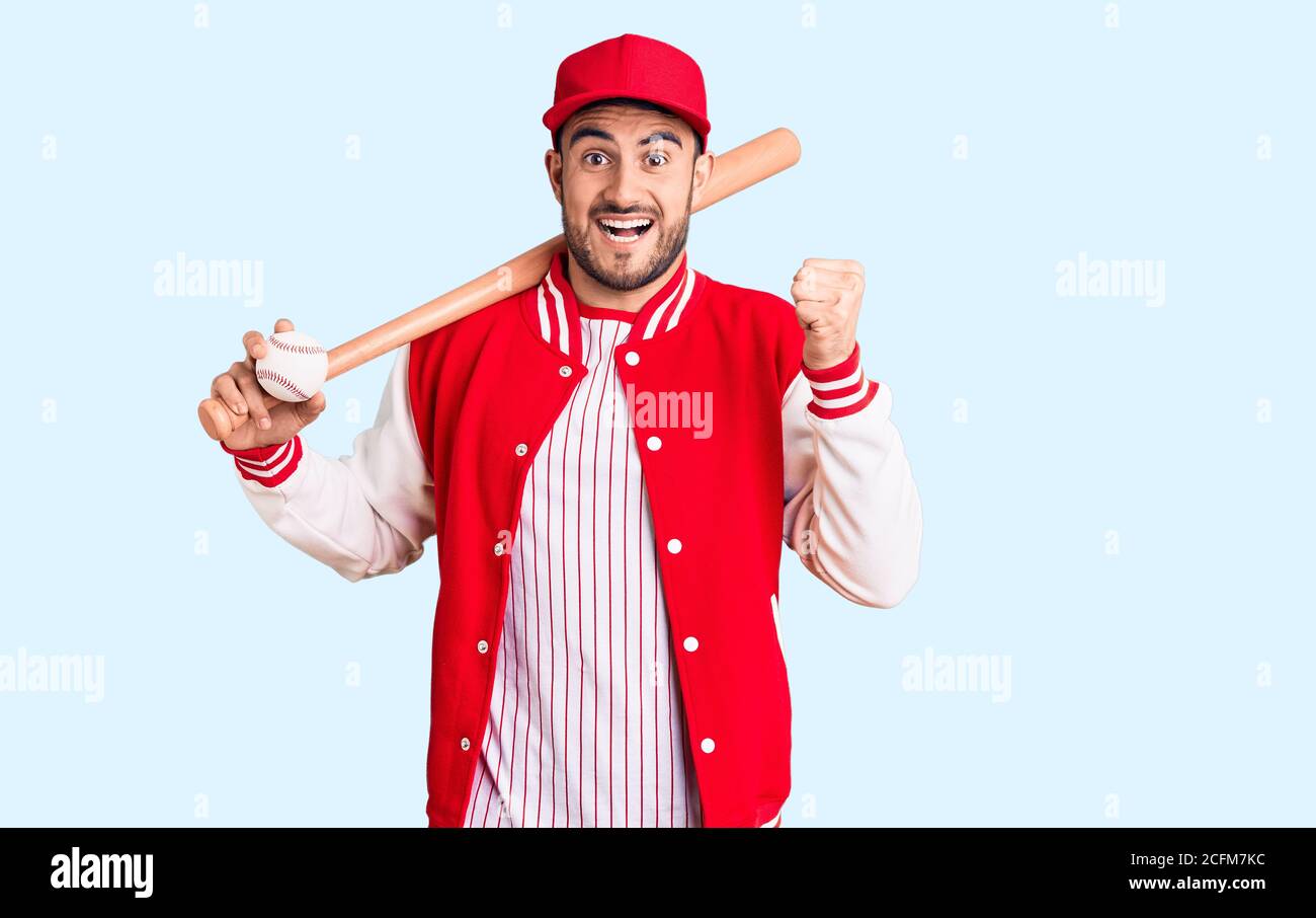 Young handsome man holding baseball bat and ball screaming proud ...