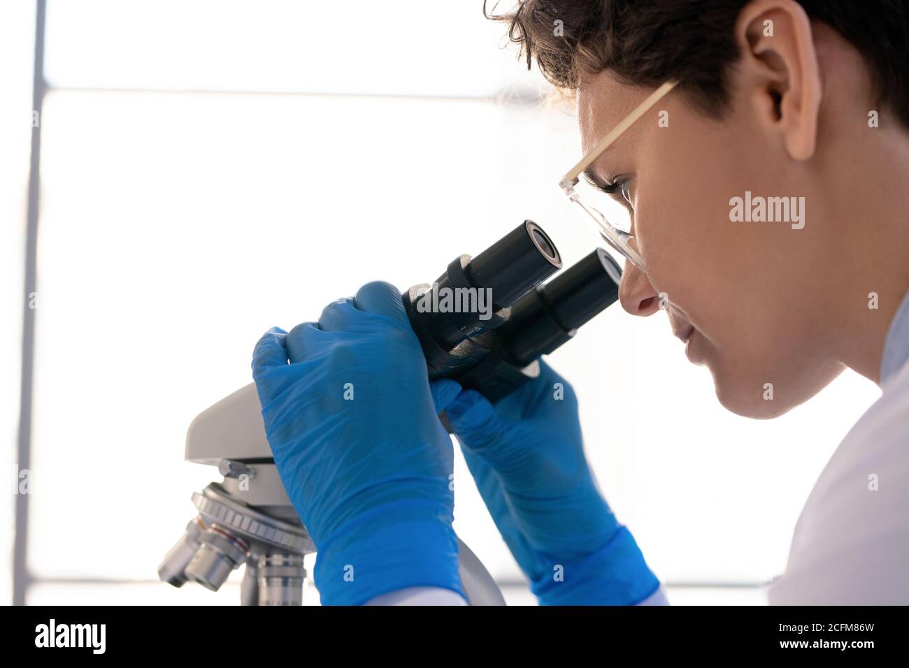 Head and gloved hands of young female scientist studying chemical ...