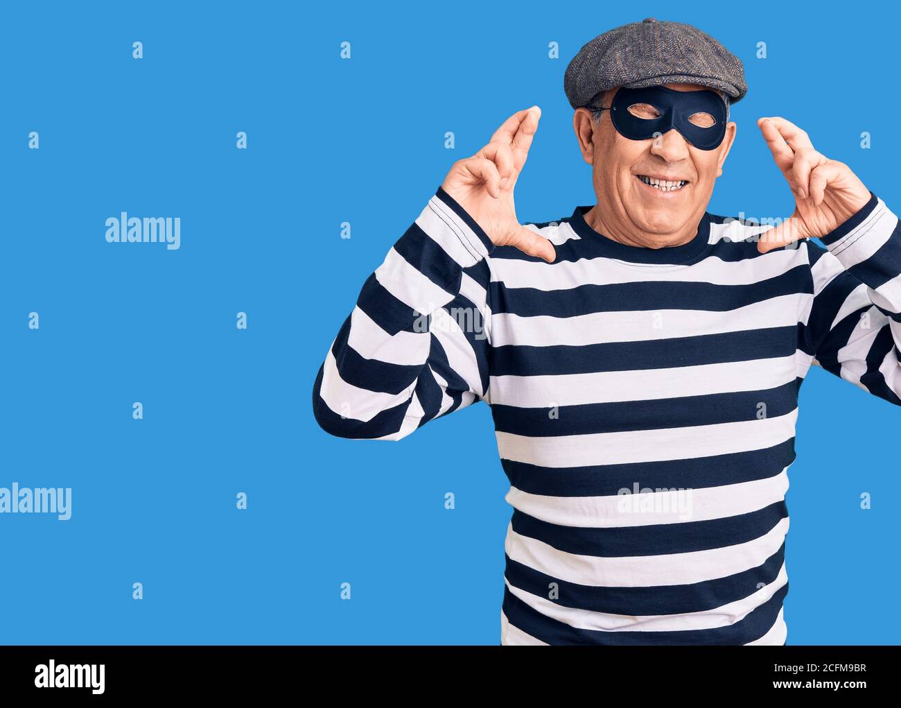 Senior handsome man wearing burglar mask and t-shirt gesturing finger ...