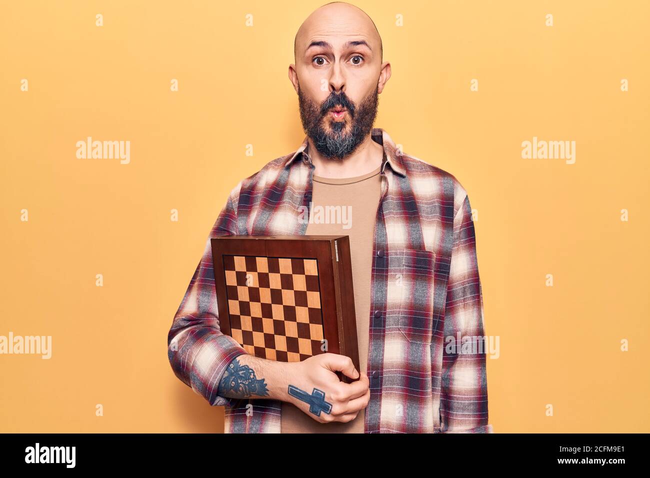 Young handsome man holding chess scared and amazed with open mouth for ...