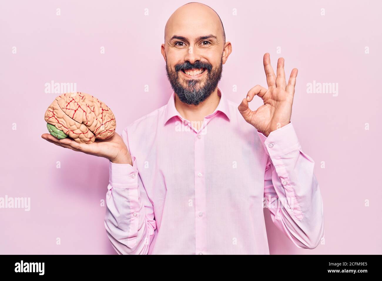Young handsome man holding brain doing ok sign with fingers, smiling ...
