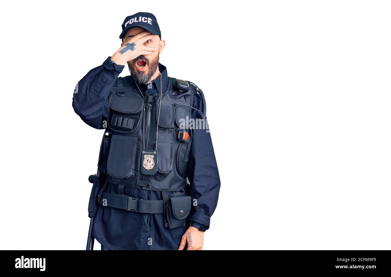 Young handsome man wearing police uniform peeking in shock covering ...