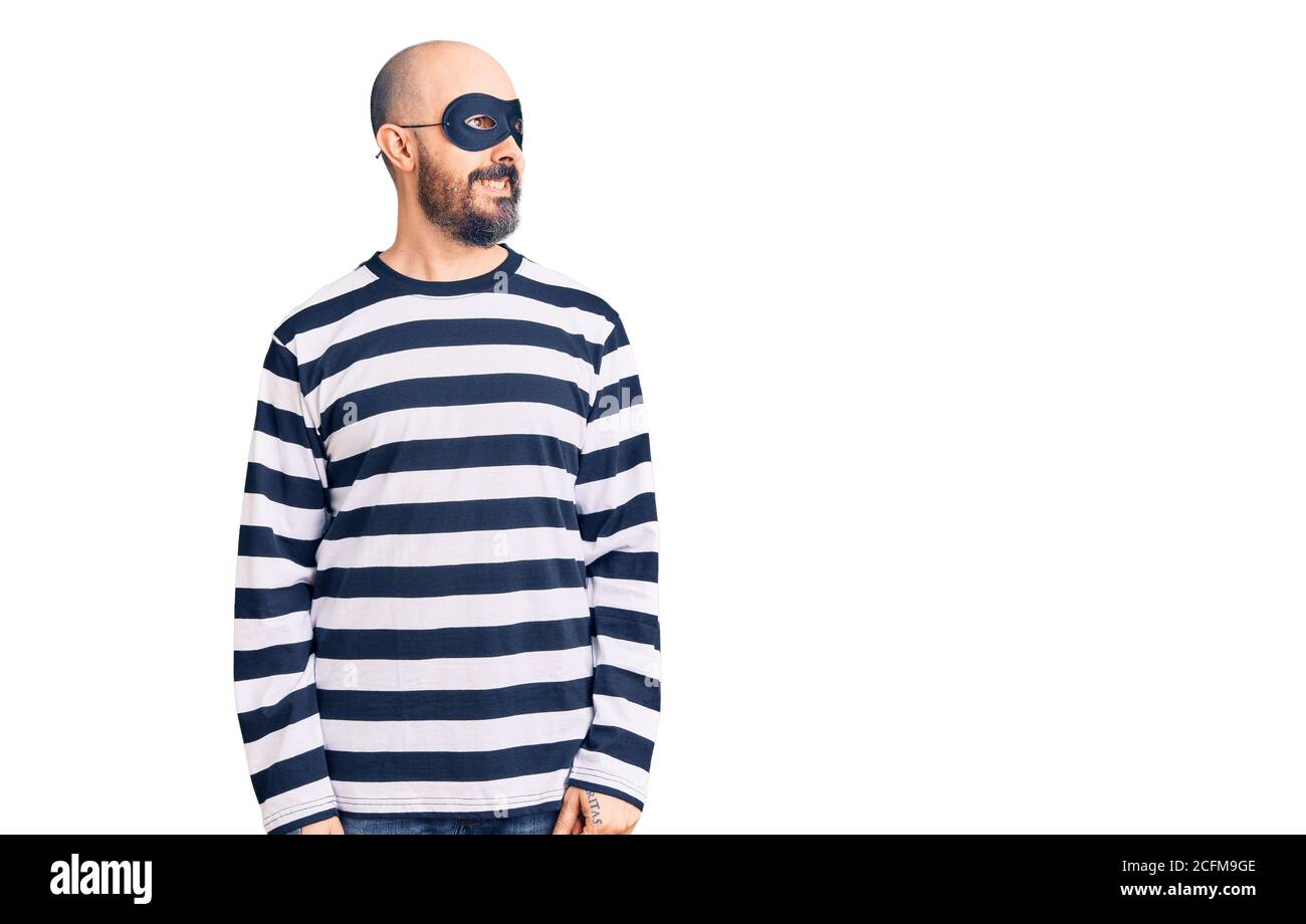 Young handsome man wearing burglar mask looking away to side with smile ...