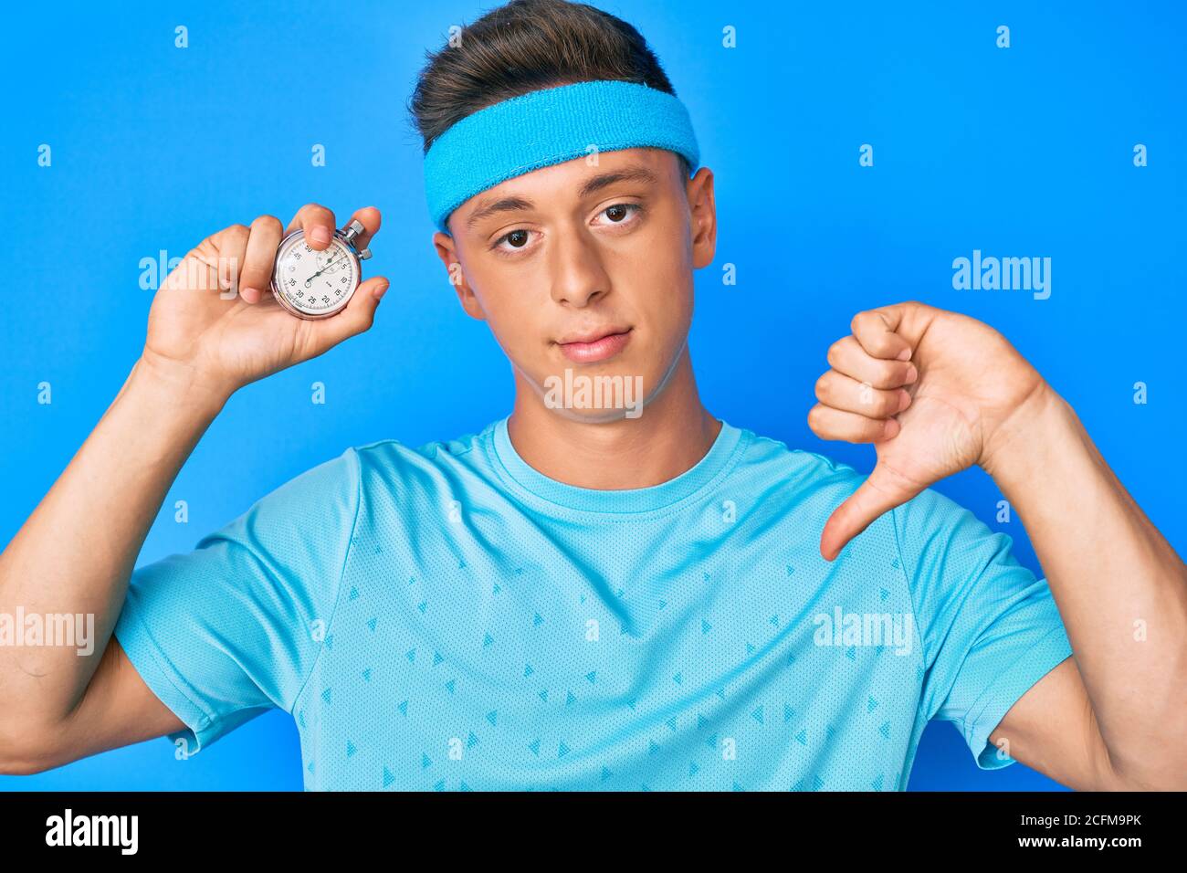 Young hispanic boy holding stopwatch with angry face, negative sign ...