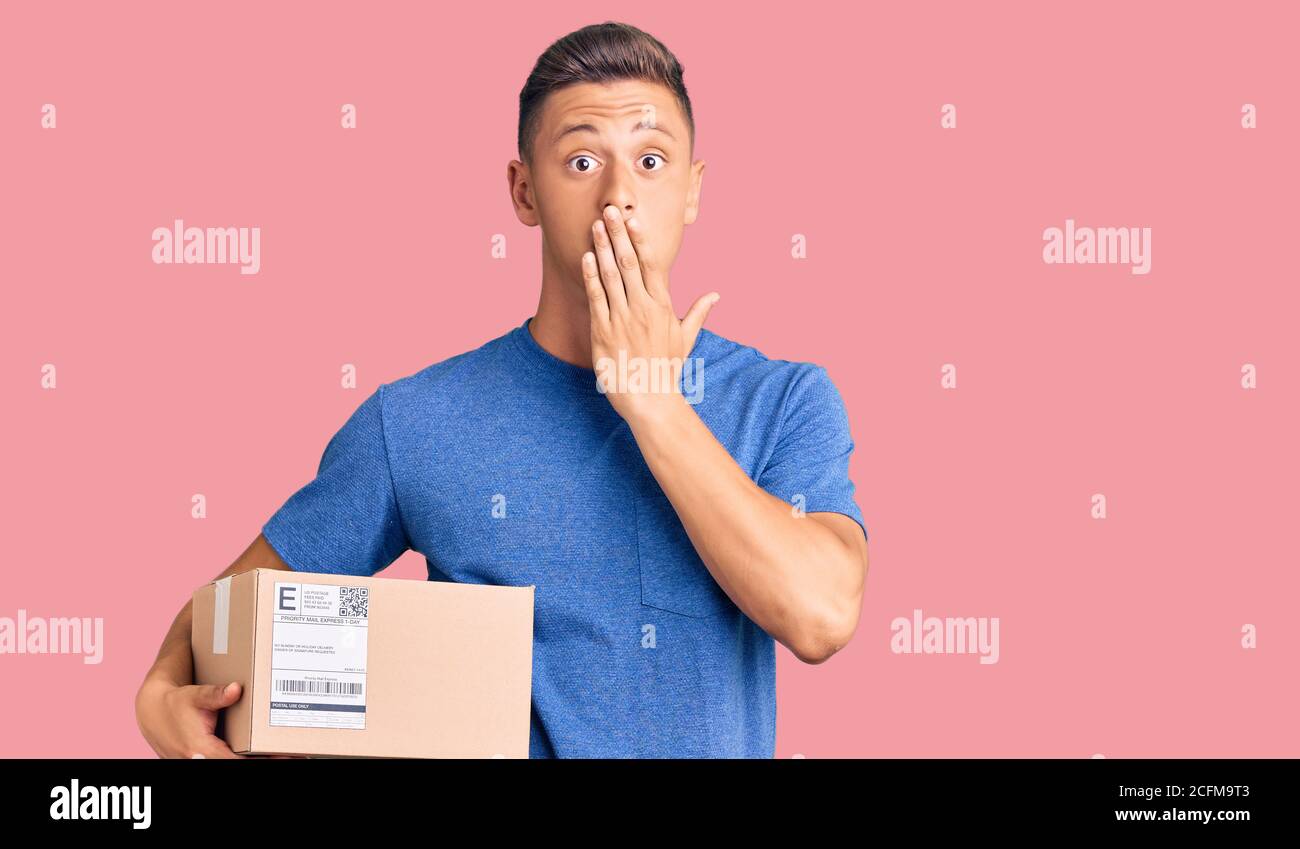 Young handsome hispanic man holding delivery package covering mouth ...