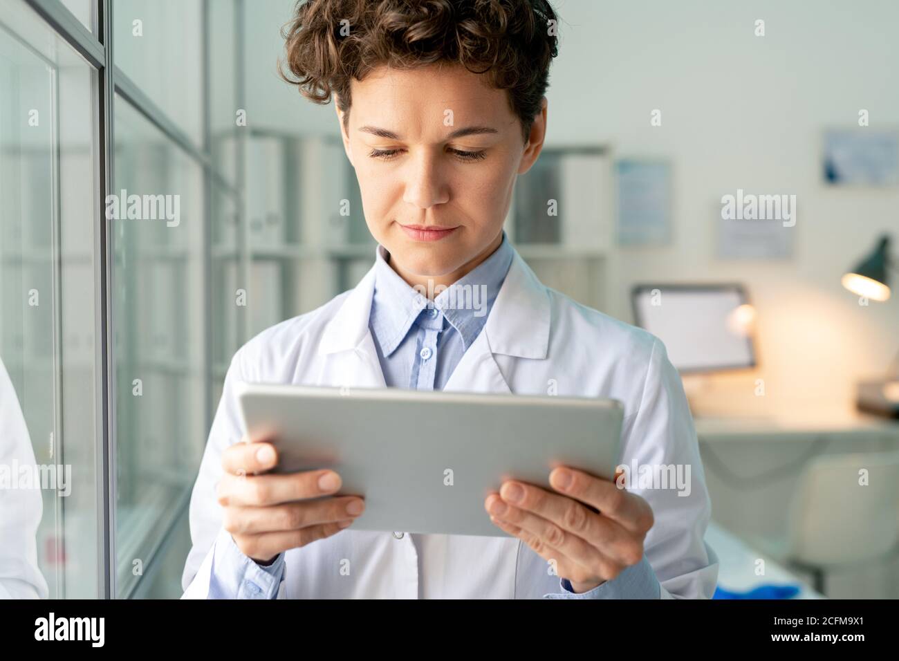 Young serious scientist or chemist in whitecoat looking through ...