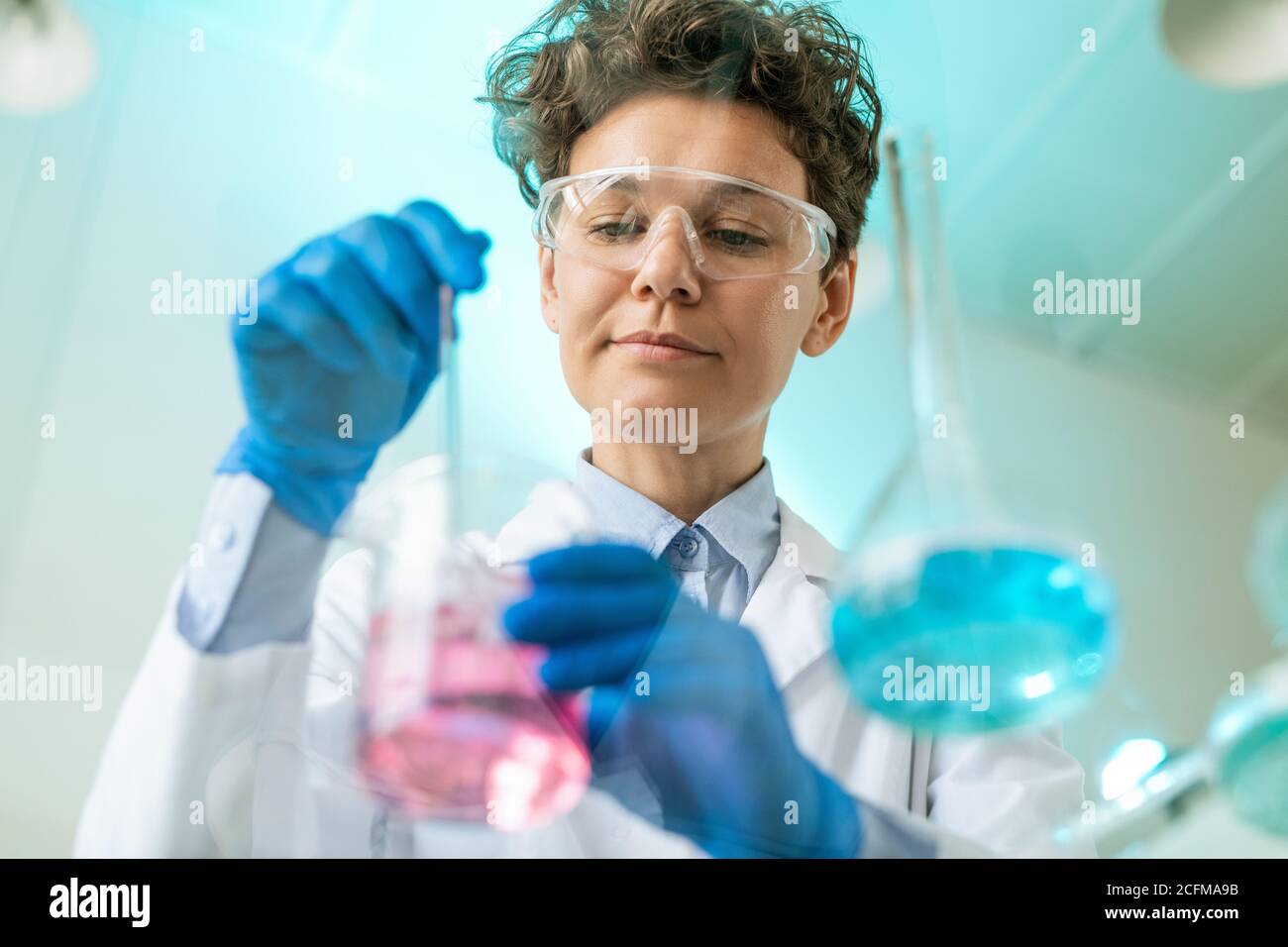 Contemporary young female scientist or researcher making chemical ...