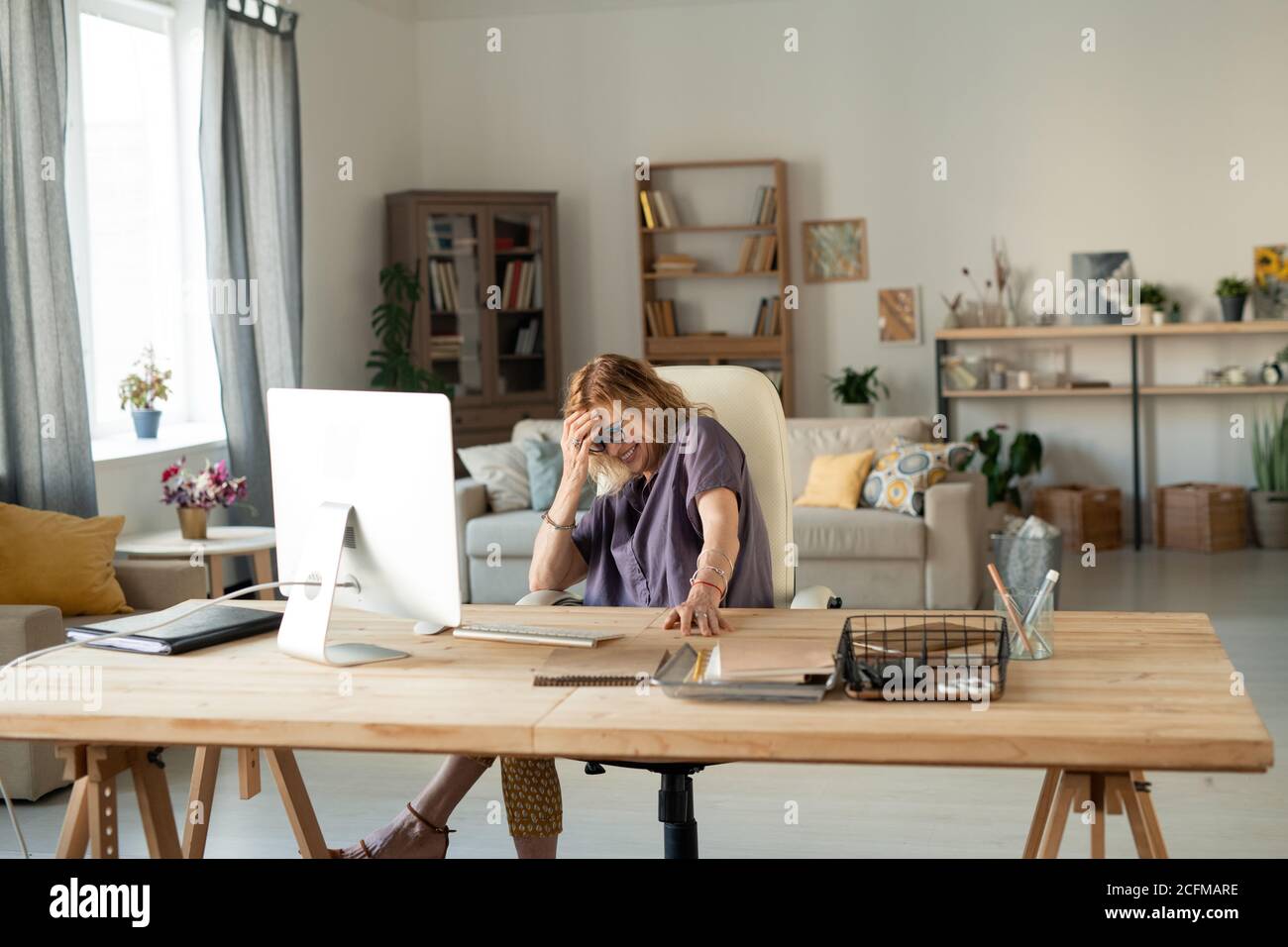 Mature blond cheerful female laughing in front of computer screen at ...