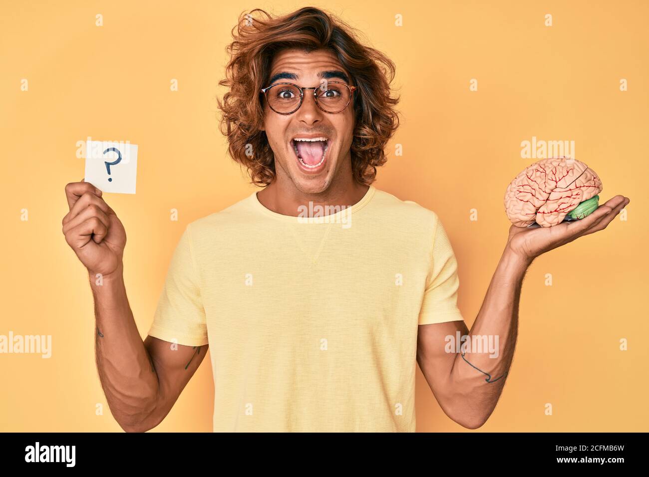 Young hispanic man holding brain and question mark celebrating crazy ...