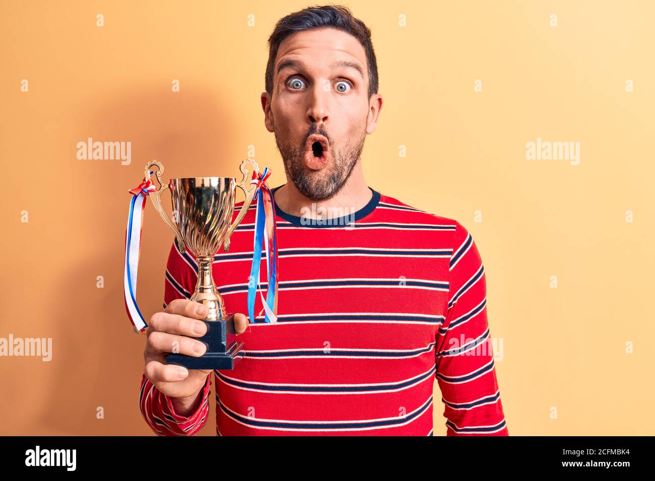 Young handsome successful man winning trophy standing over isolated ...