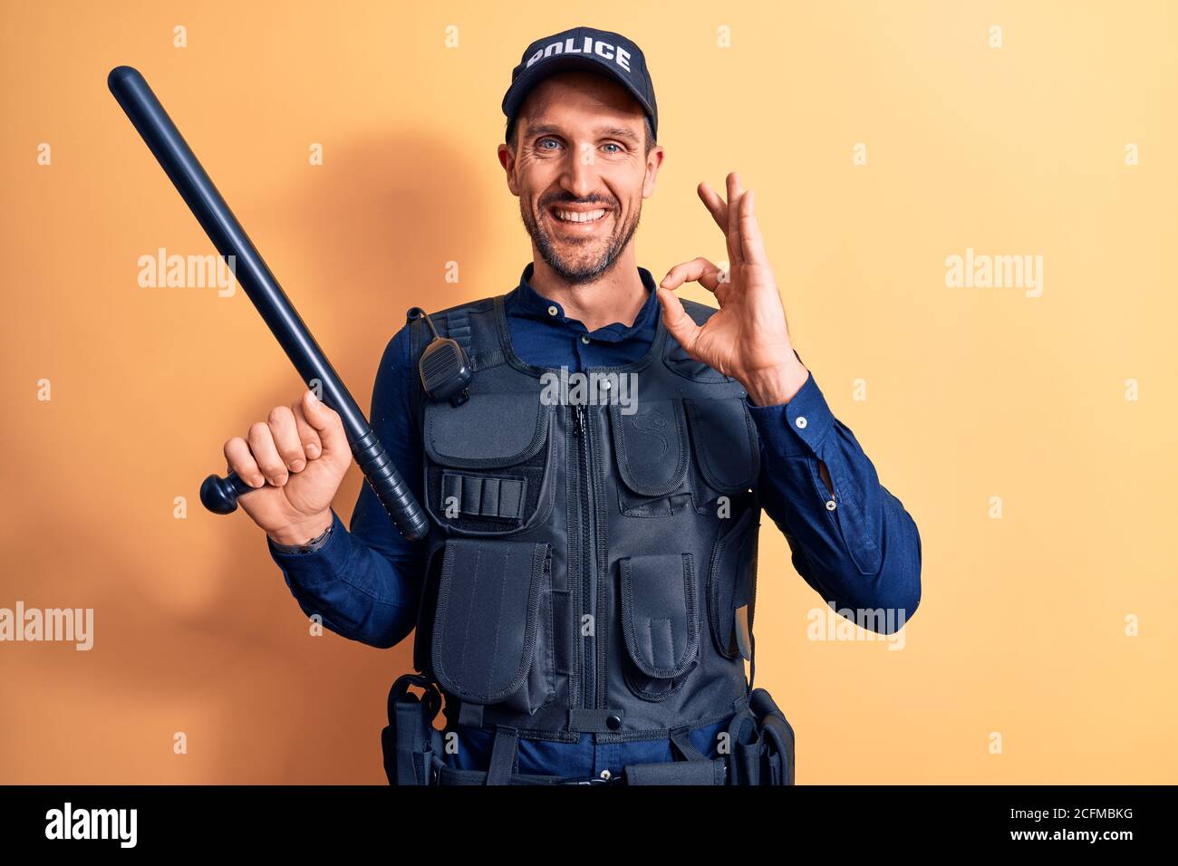 Handsome policeman wearing uniform and bulletprof holding baton over ...