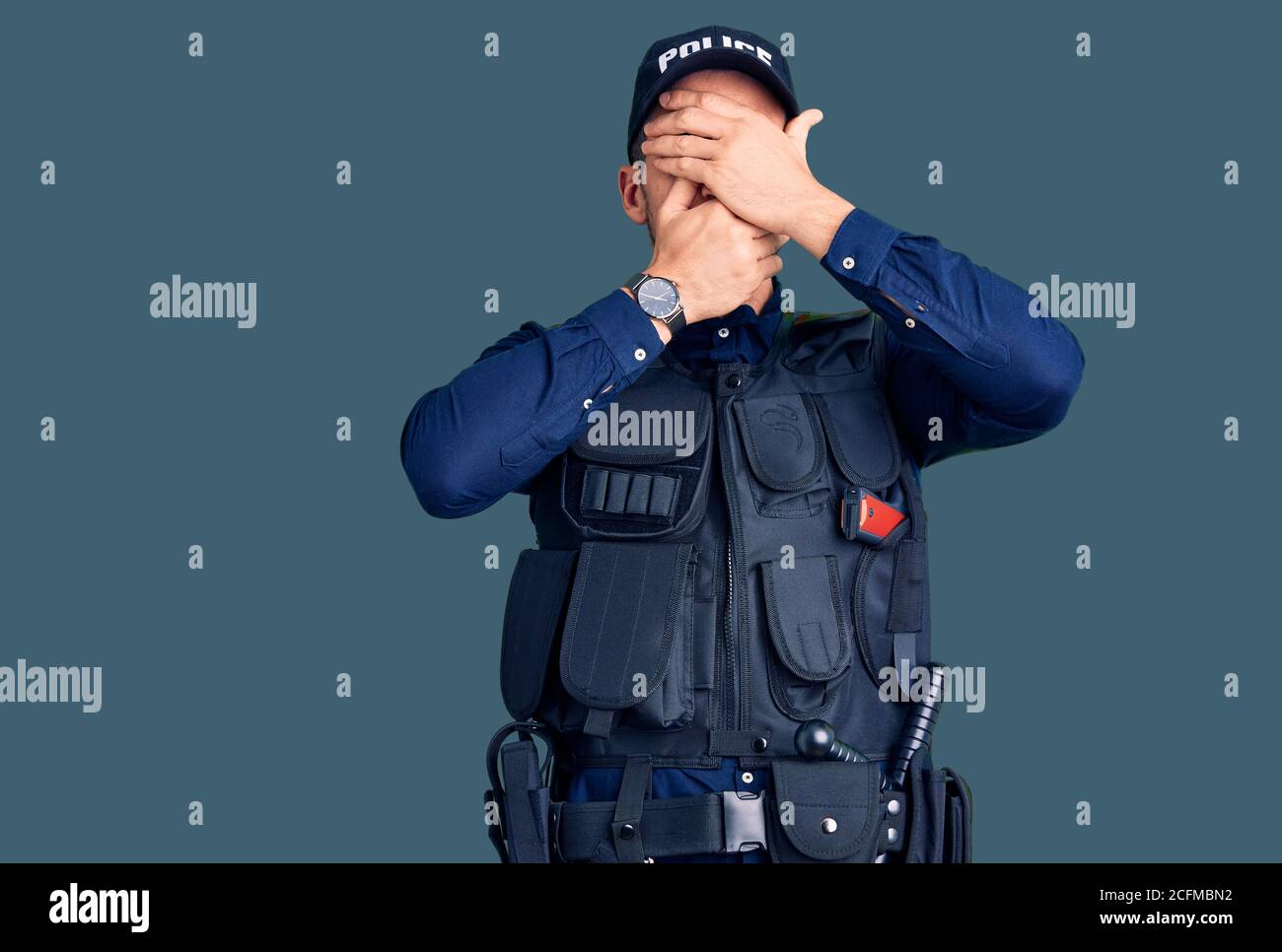 Young handsome man wearing police uniform covering eyes and mouth with ...