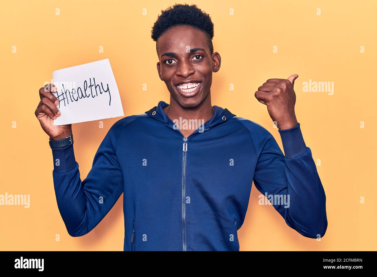 Young african american man holding healthy hashtag paper pointing thumb ...