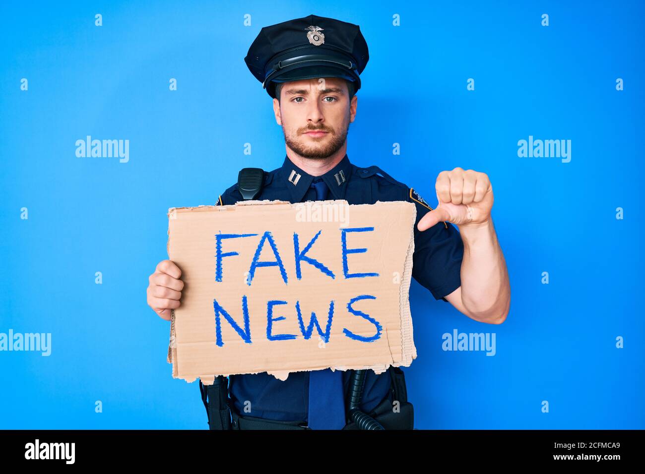 Young caucasian man wearing police uniform holding fake news banner ...