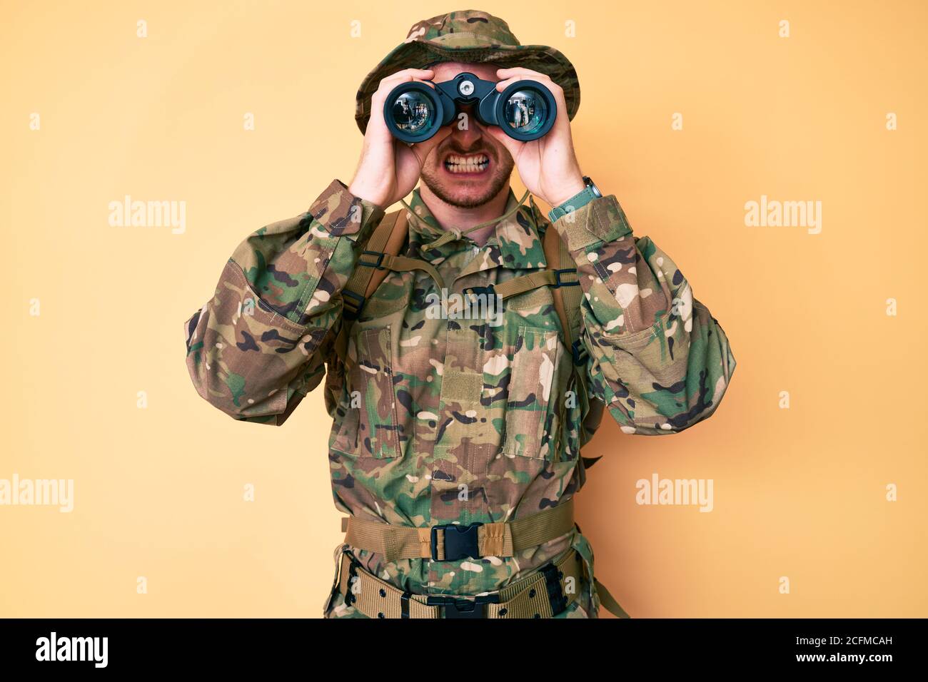 Young caucasian man wearing camouflage army uniform using binoculars ...