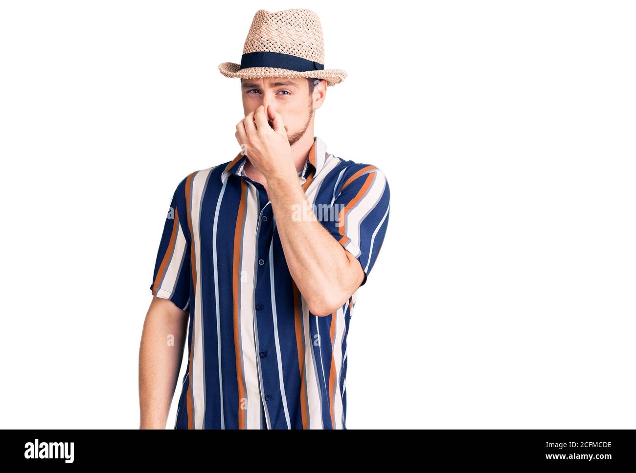 Young handsome caucasian man wearing summer hat smelling something ...