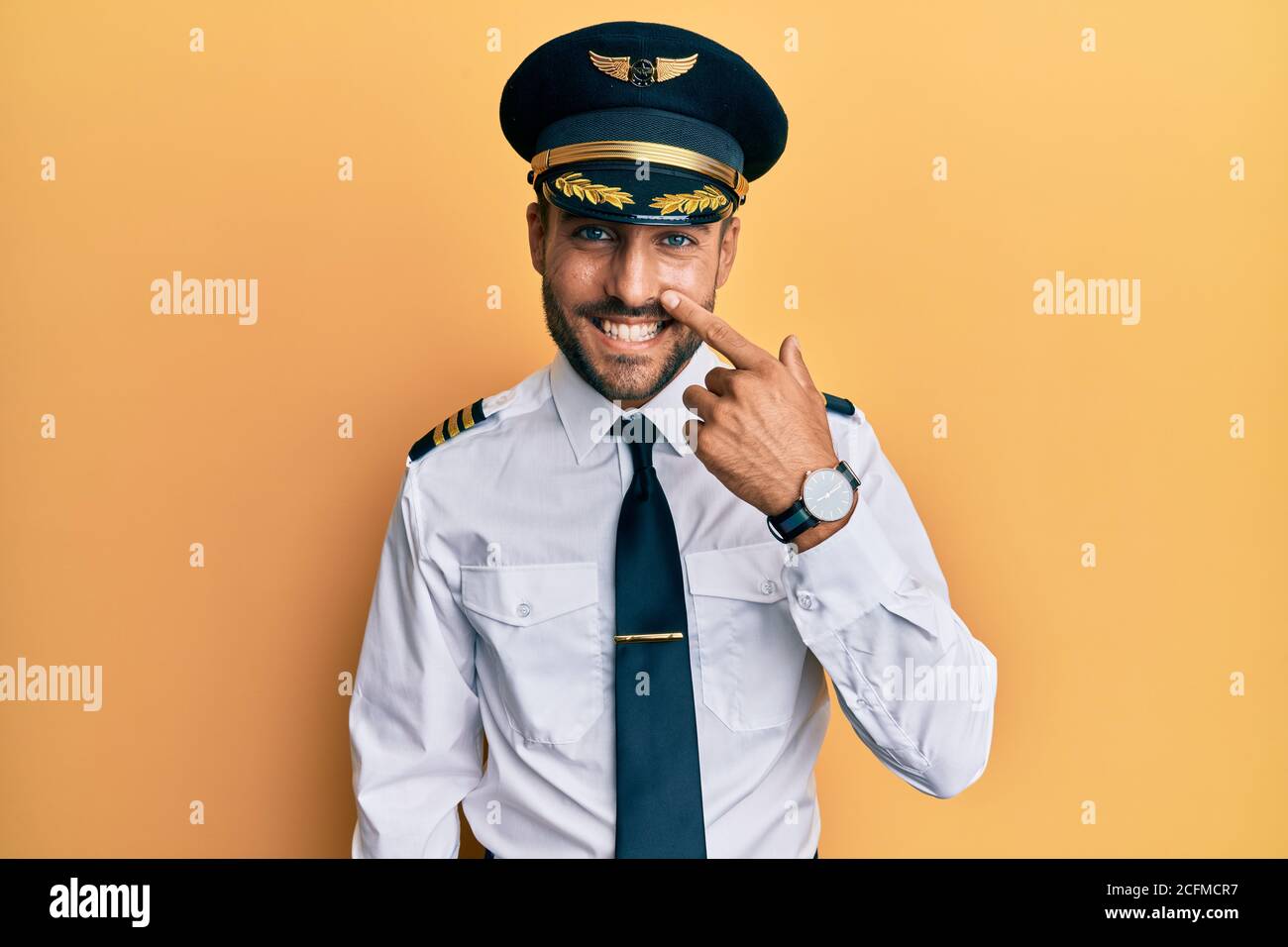 Handsome hispanic man wearing airplane pilot uniform pointing with hand ...