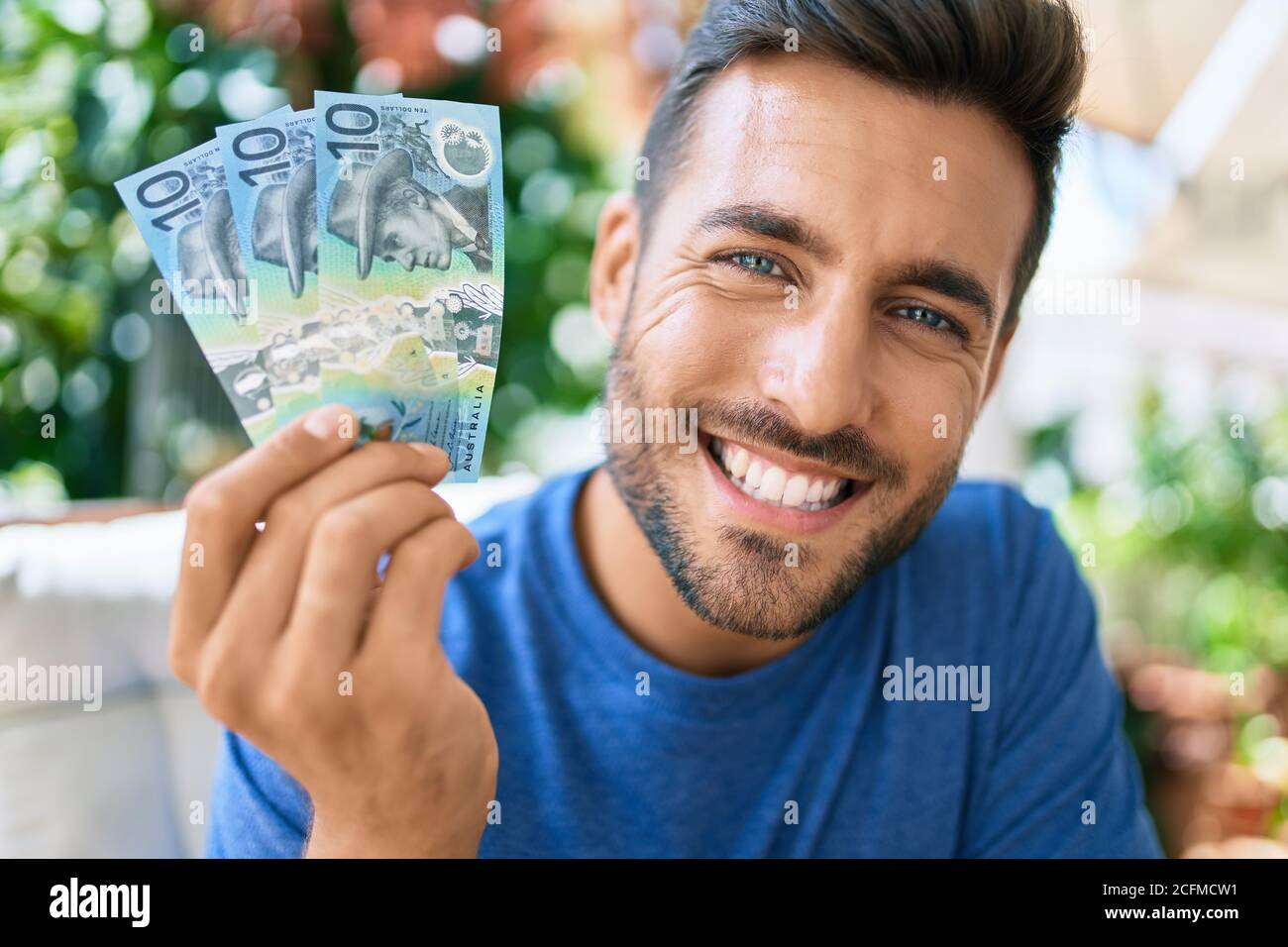 Young hispanic man smiling happy holding australian dollars banknotes ...