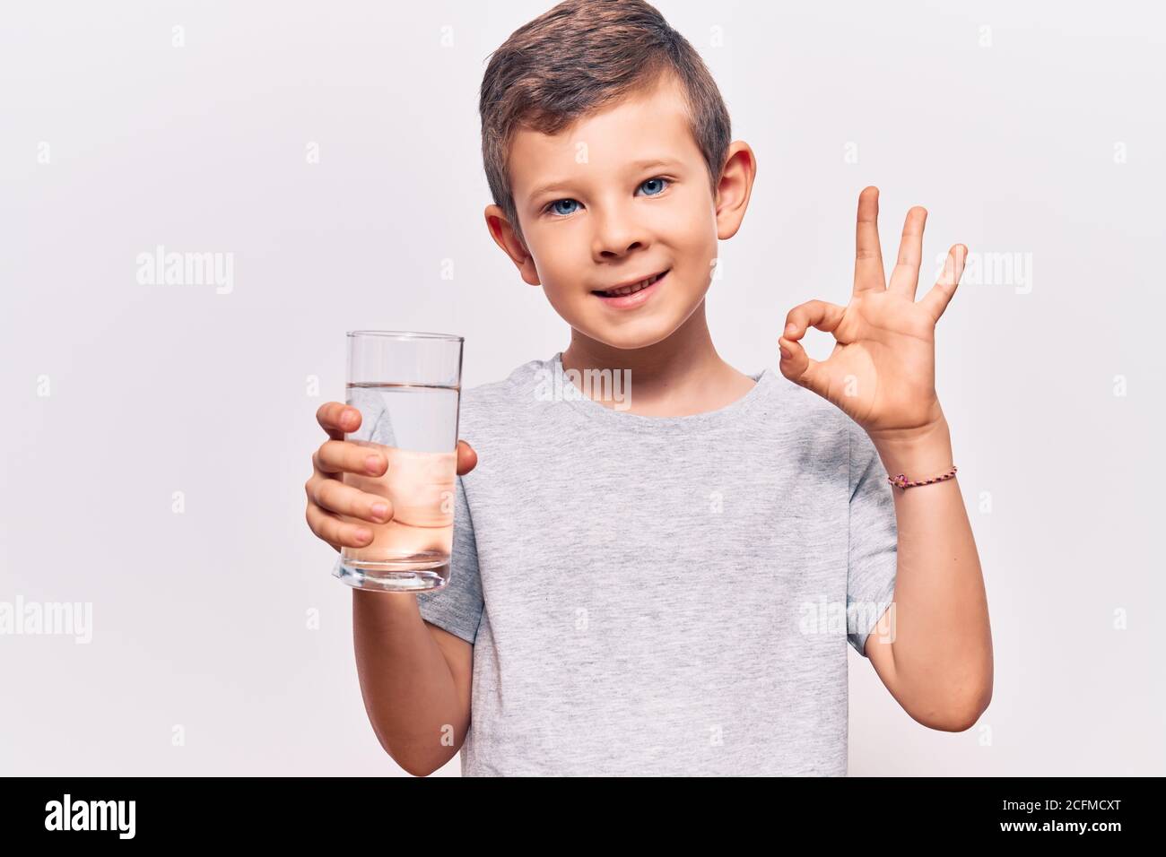 Cute blond kid drinking glass of water doing ok sign with fingers ...