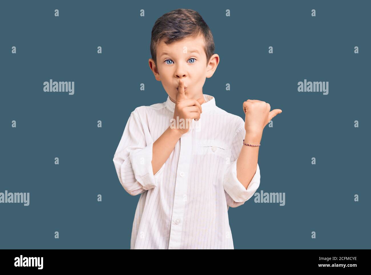 Cute blond kid wearing elegant shirt asking to be quiet with finger on ...