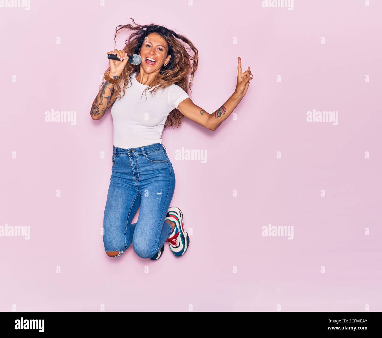 Young beautiful curly singer woman with tattoo smiling happy. Jumping ...