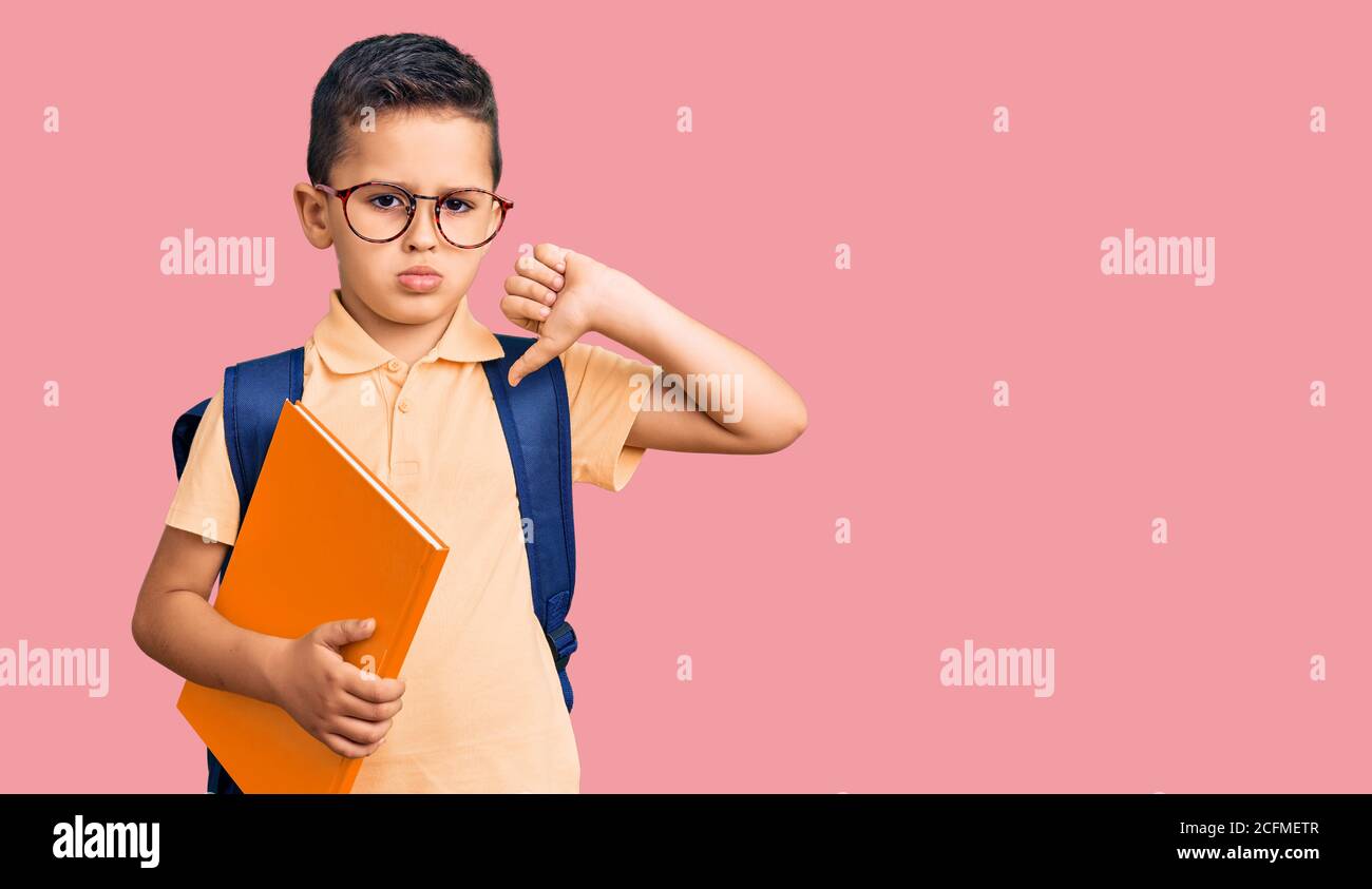 Little cute boy kid wearing school bag and holding book with angry face ...