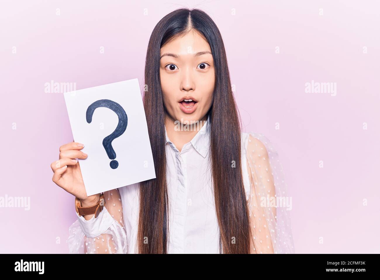 Young beautiful chinese woman holding question mark scared and amazed ...