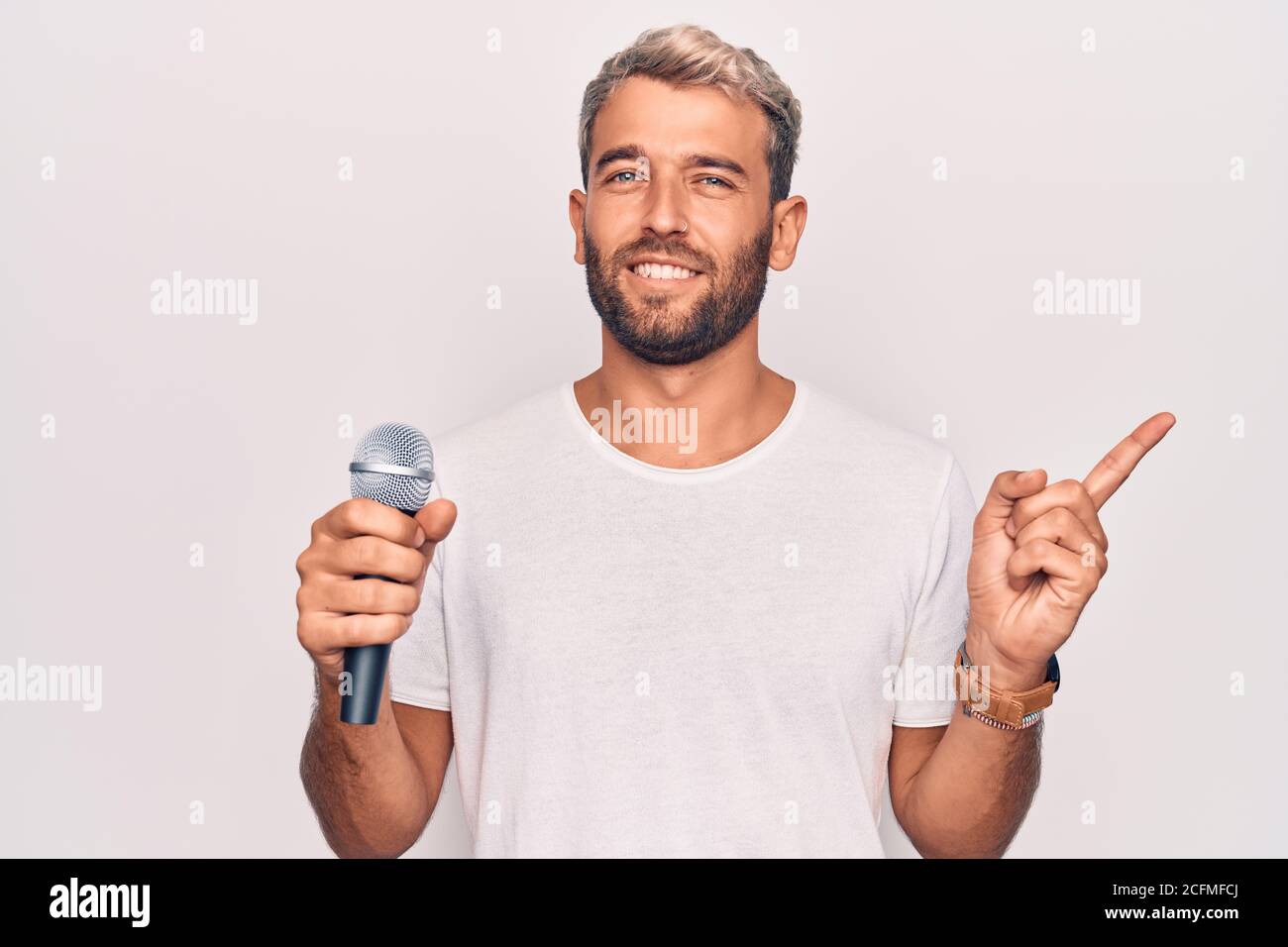 Handsome blond singer man with beard singing song using microphone over white background smiling ...