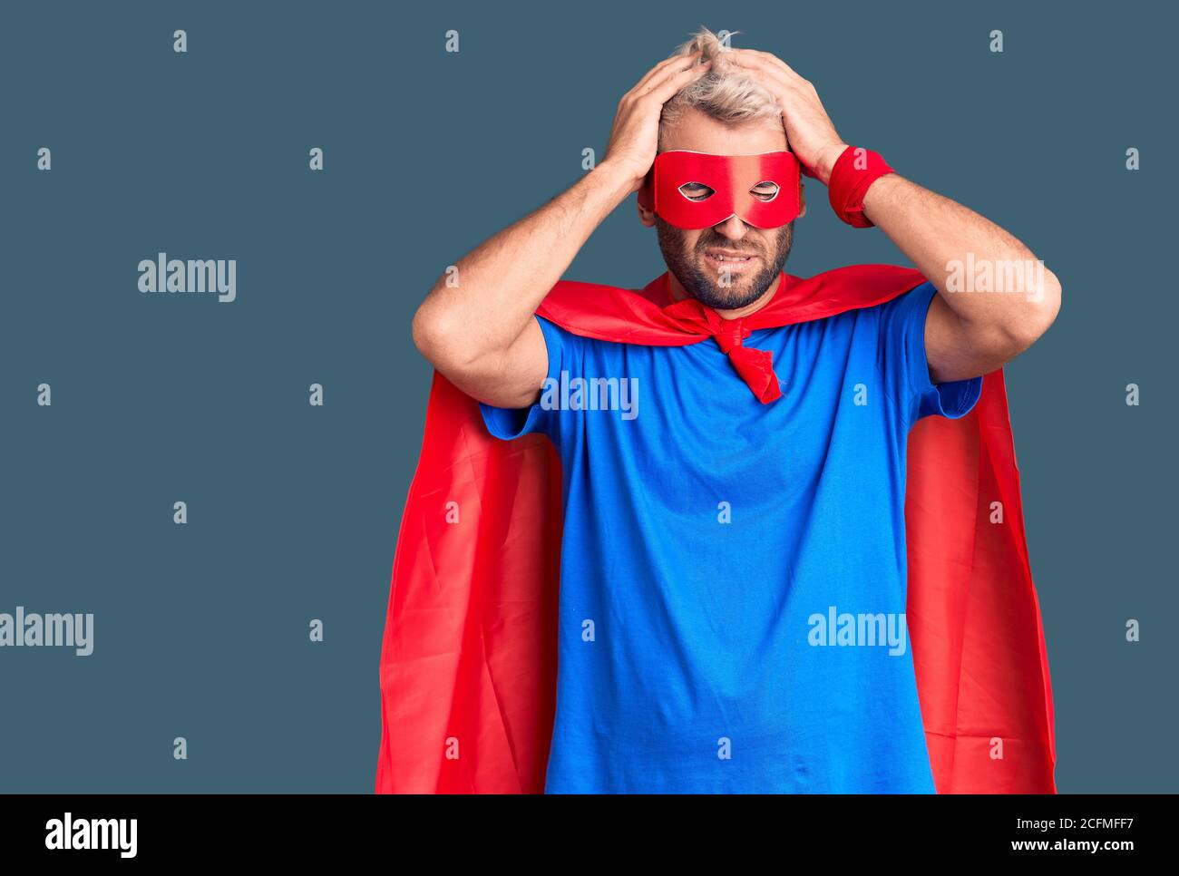Young blond man wearing super hero custome suffering from headache ...