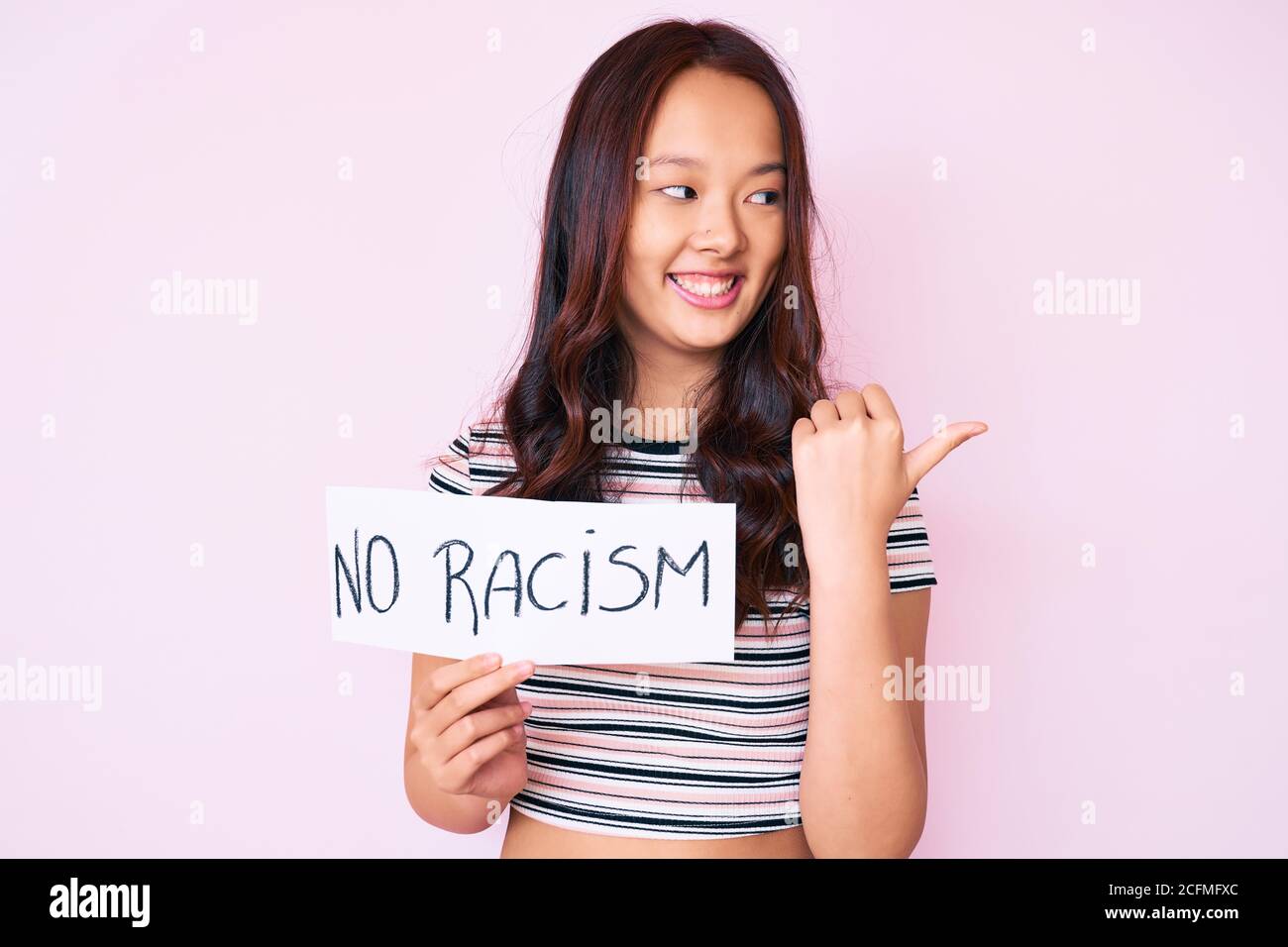 Young beautiful chinese girl holding no racism banner pointing thumb up ...