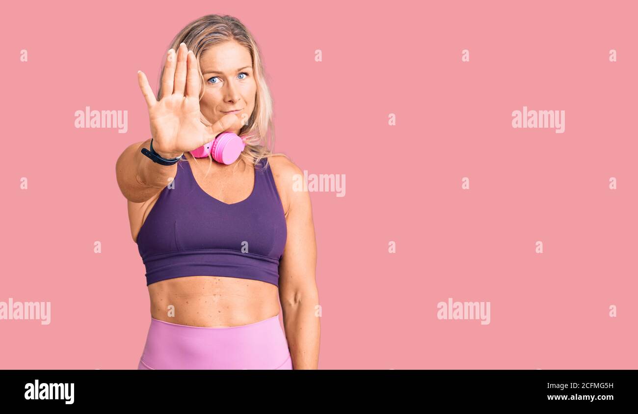 Middle age fit blonde woman wearing gym clothes and using headphones ...