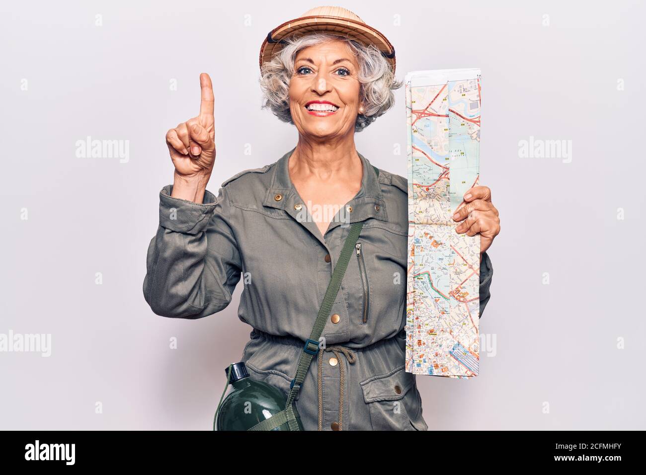 Senior grey-haired woman wearing explorer hat holding map surprised ...