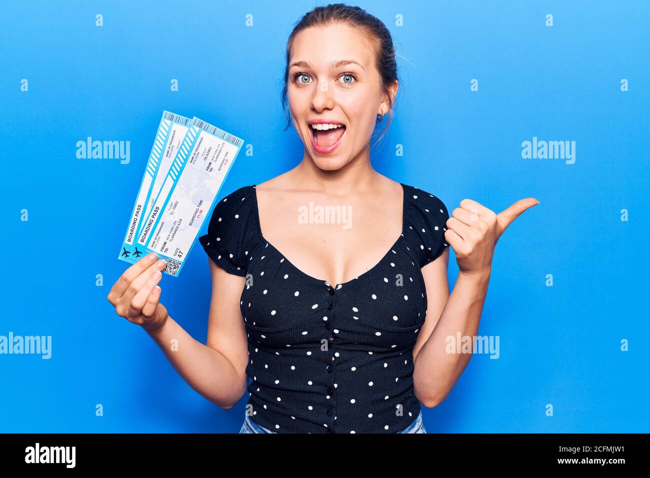 Young beautiful blonde woman holding boarding pass pointing thumb up to ...