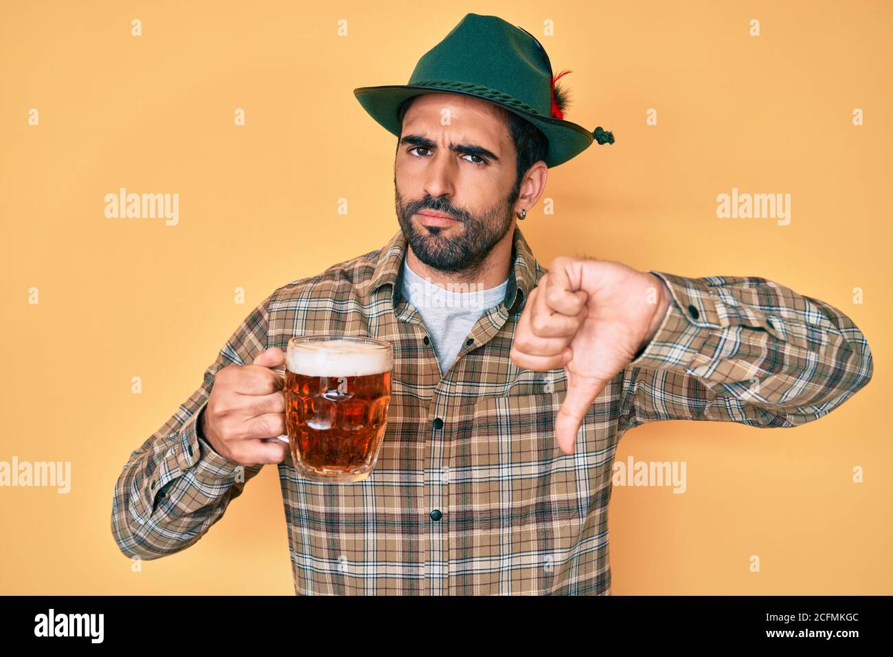 Handsome hispanic man with beard wearing octoberfest hat drinking beer ...