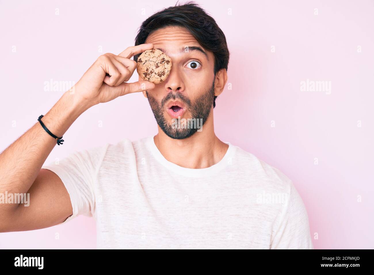 Handsome hispanic man holding cookie scared and amazed with open mouth ...