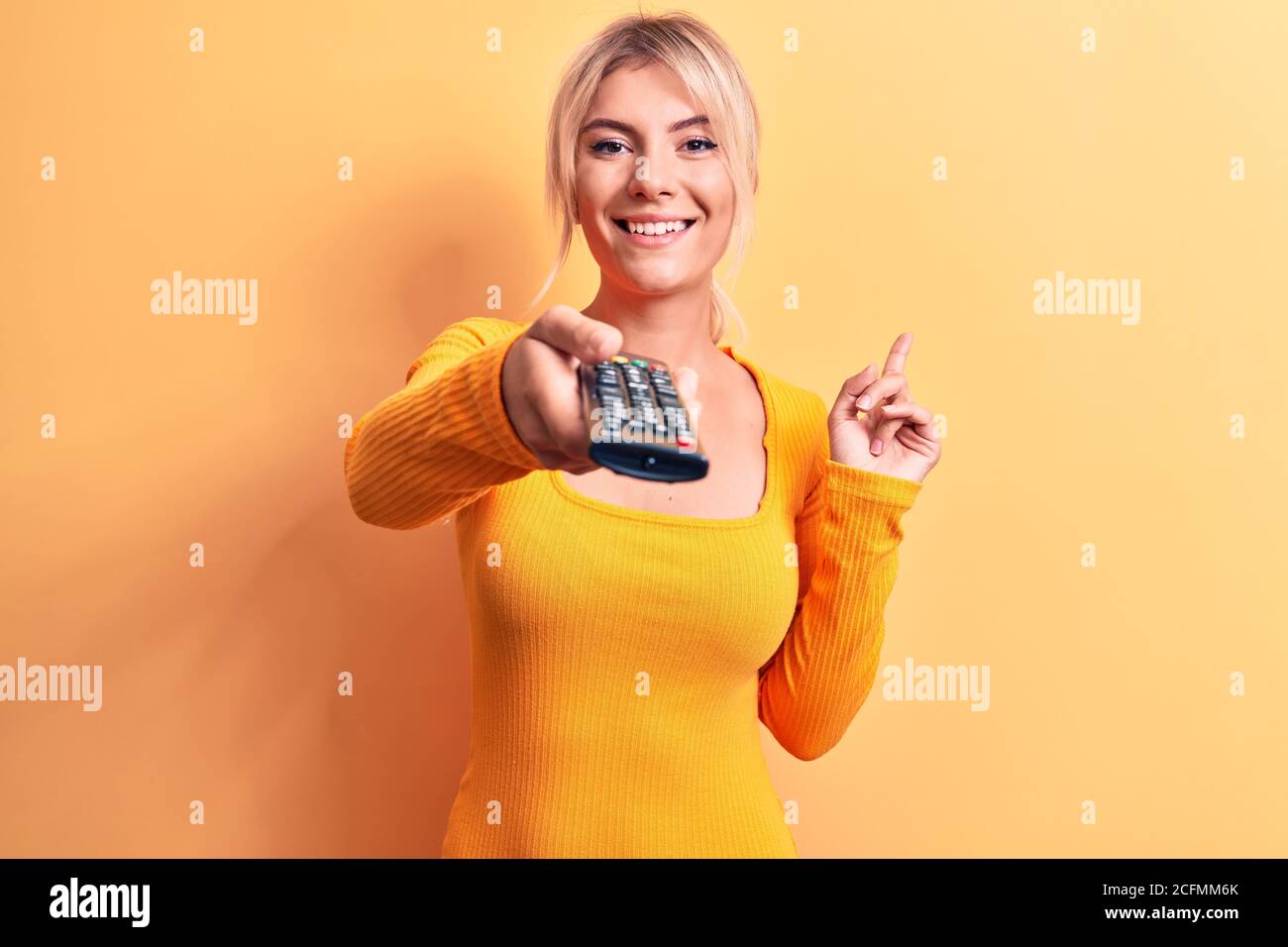 Blonde woman changing tv channel using television remote control over ...