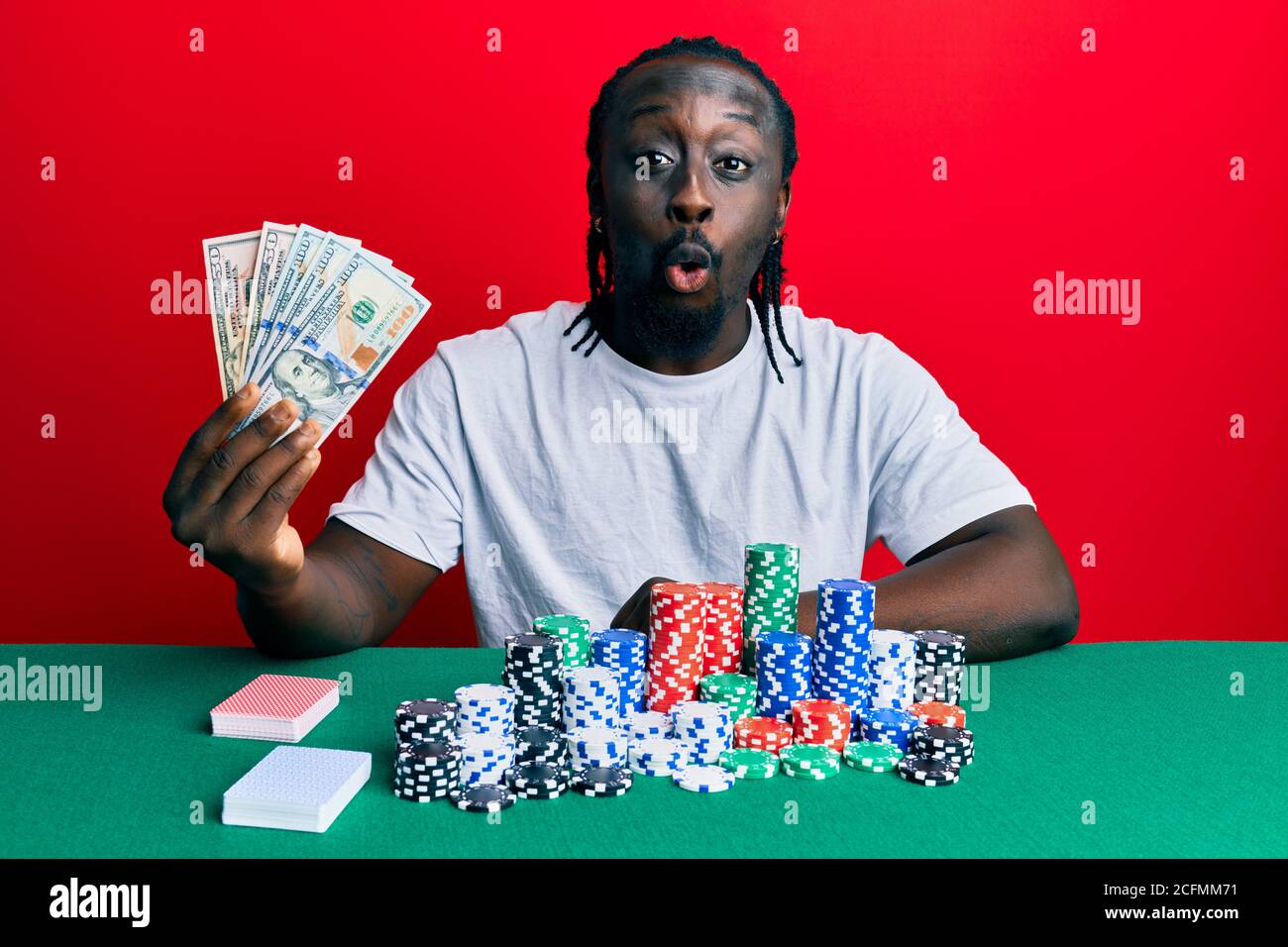 Handsome young black man playing poker holding 100 dollars banknotes ...