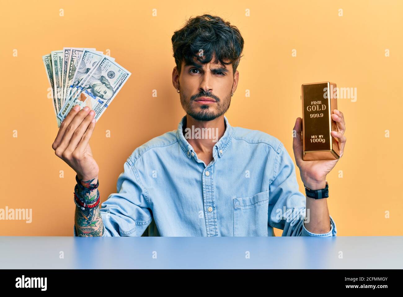 Young hispanic man holding dollars and gold ingot skeptic and nervous ...