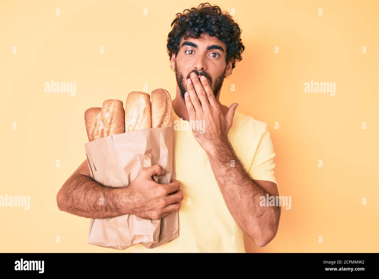 Handsome young man with curly hair and bear holding paper bag with ...