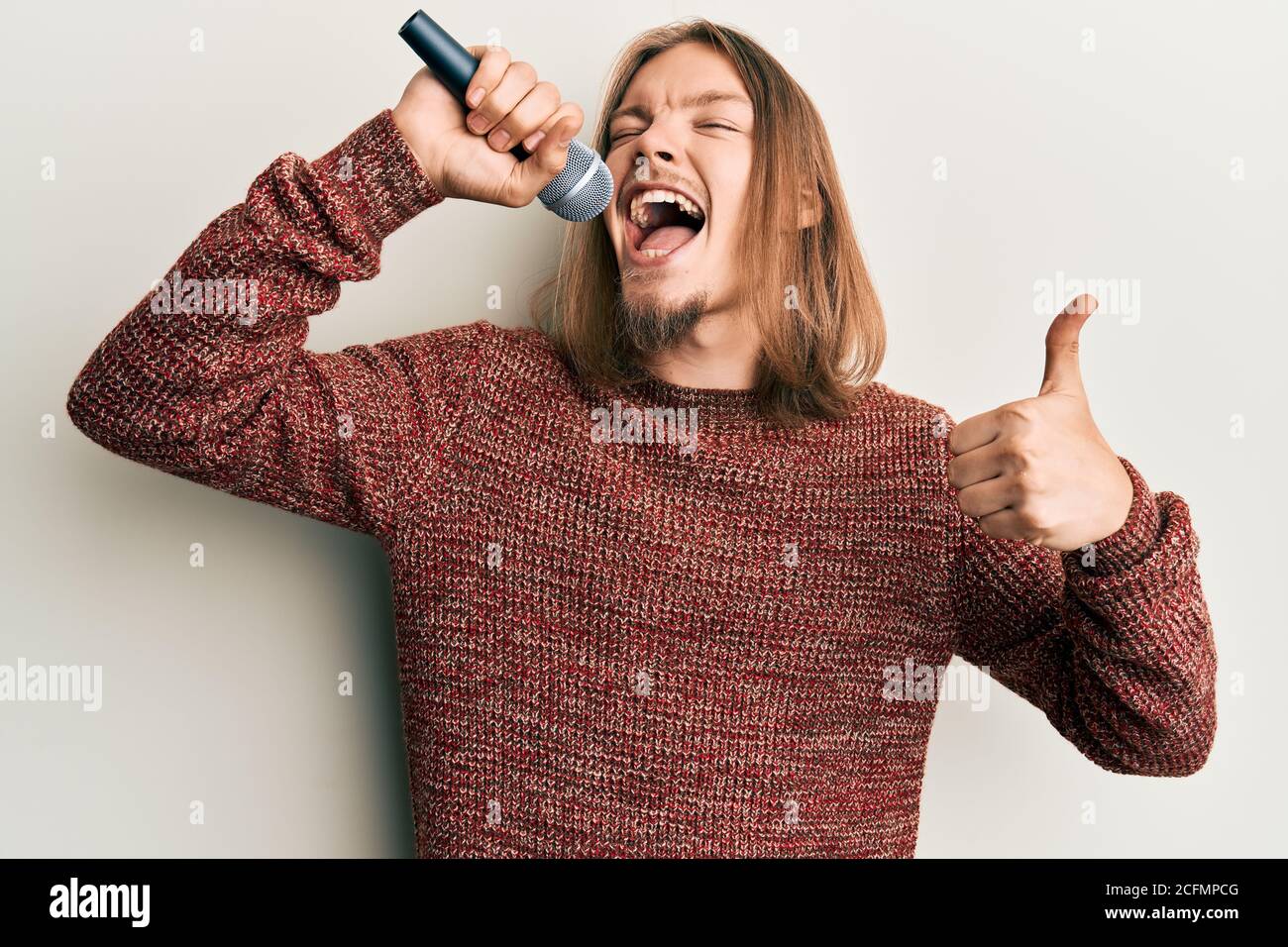 Handsome caucasian man with long hair singing song using microphone ...
