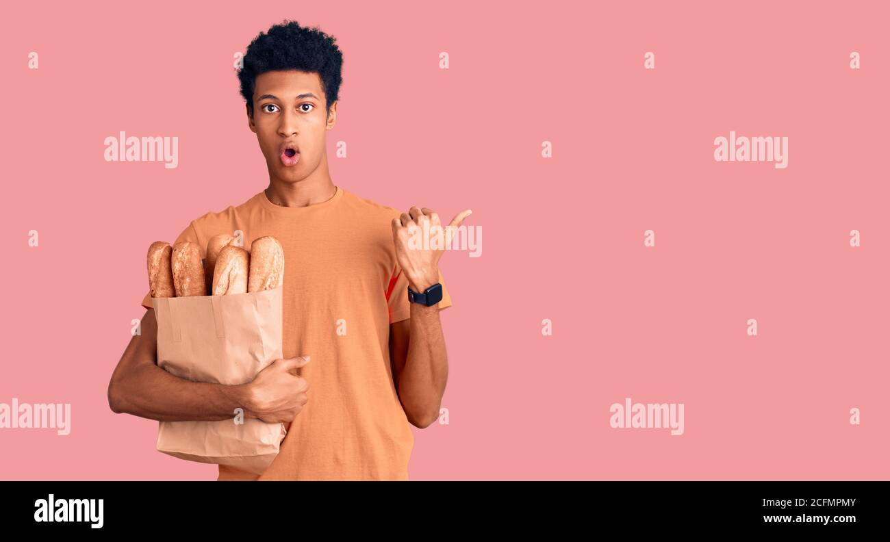 Young african american man holding paper bag with bread surprised ...