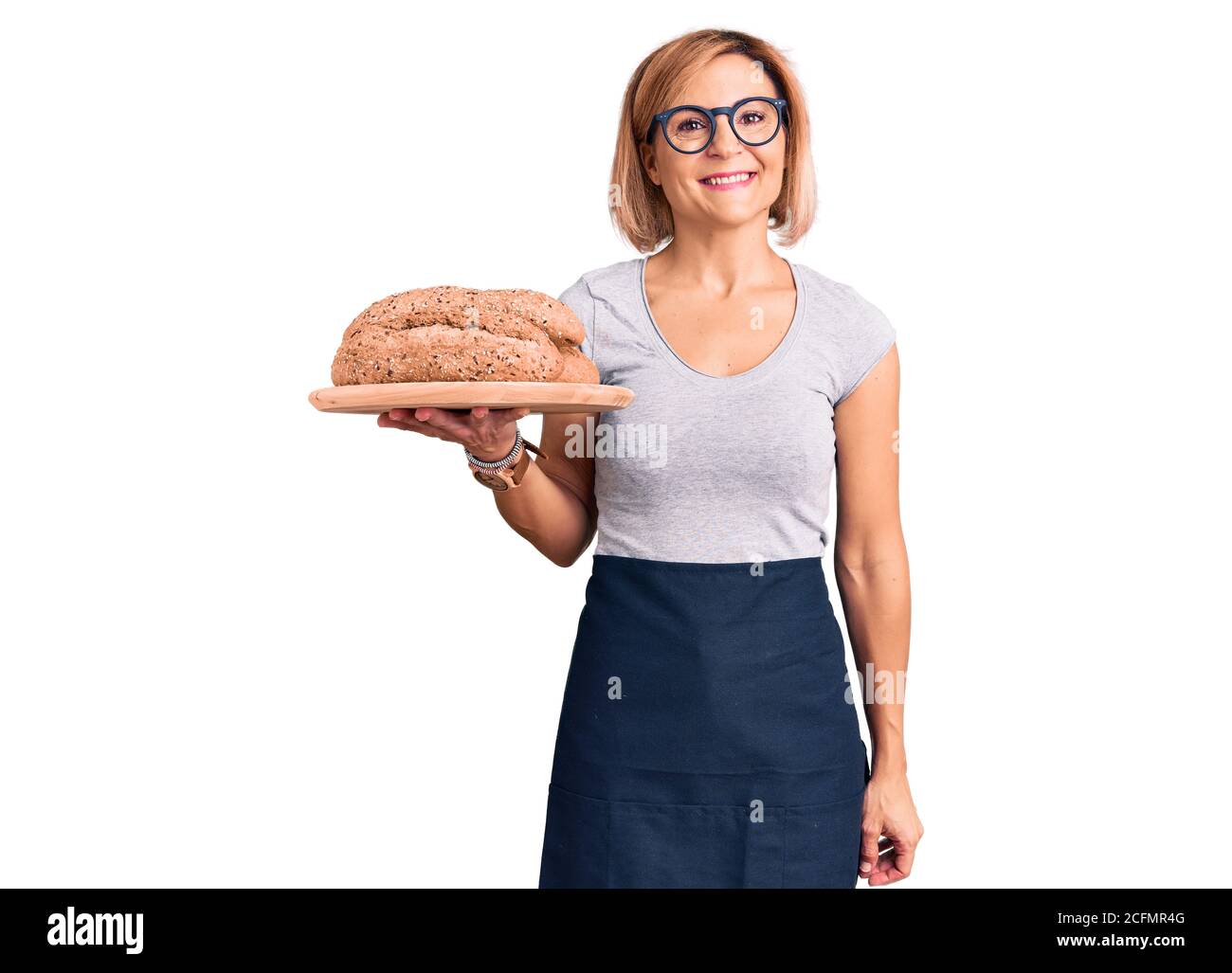 Young blonde woman holding wholemeal bread looking positive and happy ...