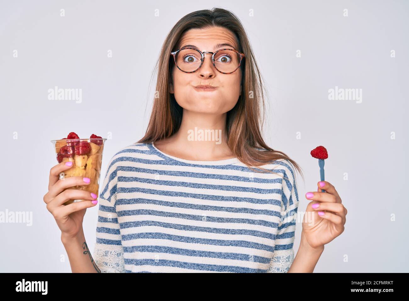 Beautiful caucasian woman eating fresh and healthy fruit puffing cheeks ...