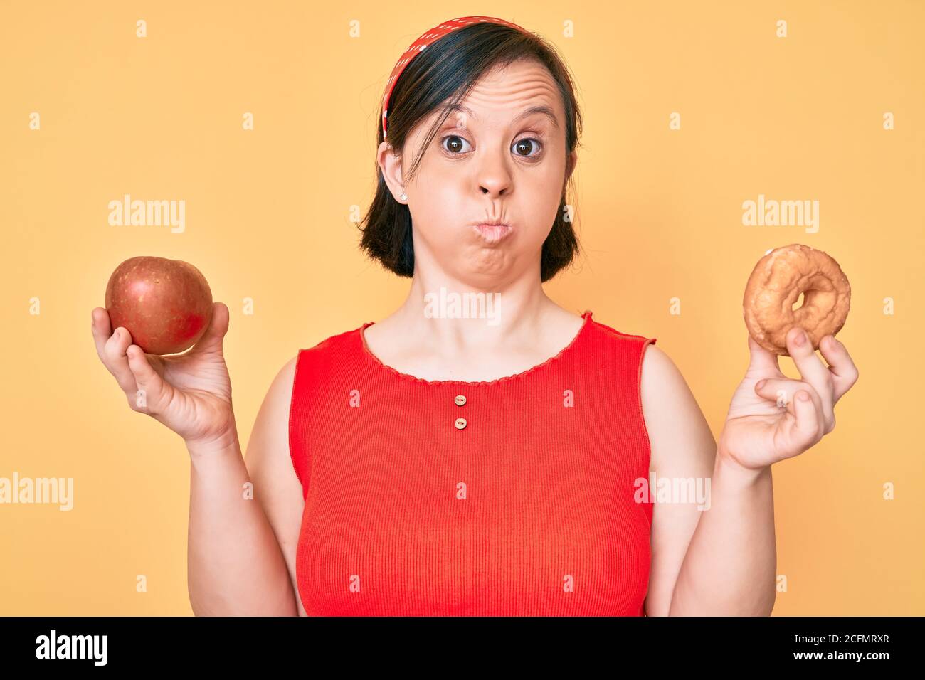 Brunette woman with down syndrome holding red apple and donut sitting ...