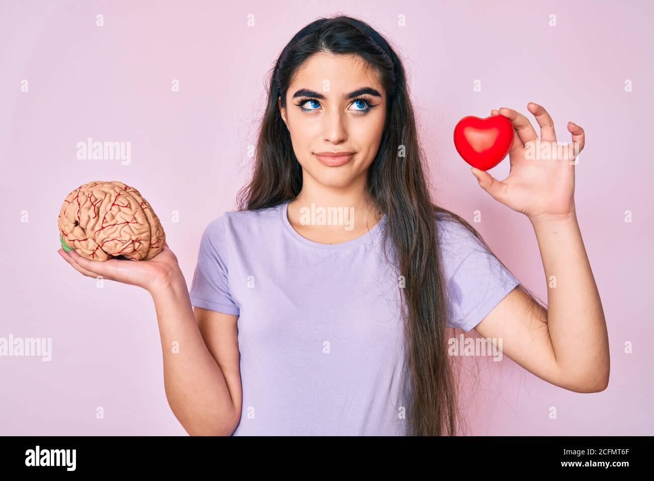 Brunette teenager girl holding brain and heart smiling looking to the ...