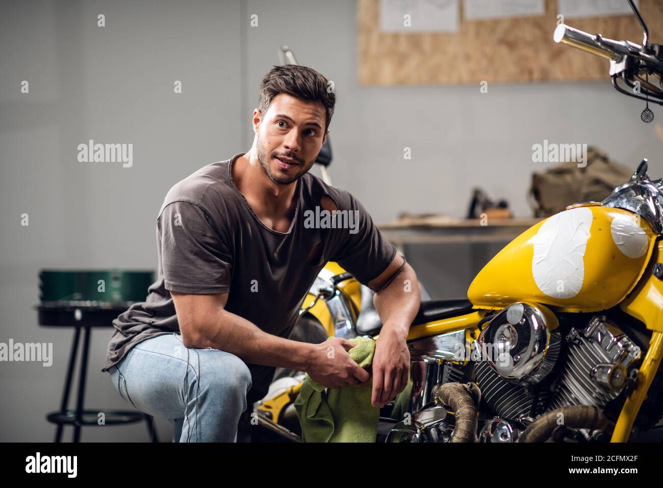 A handsome young male biker in his garage is preparing his motorcycle ...